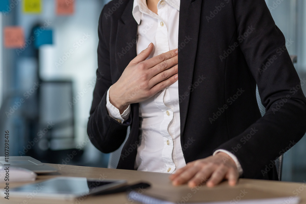 Businesswoman in smart office attire sits at desk with hand on chest ...