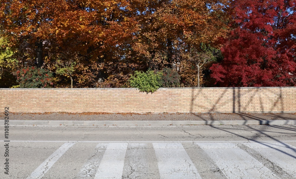 Brick fence with garden on behind colored with autumn leaves of trees ...
