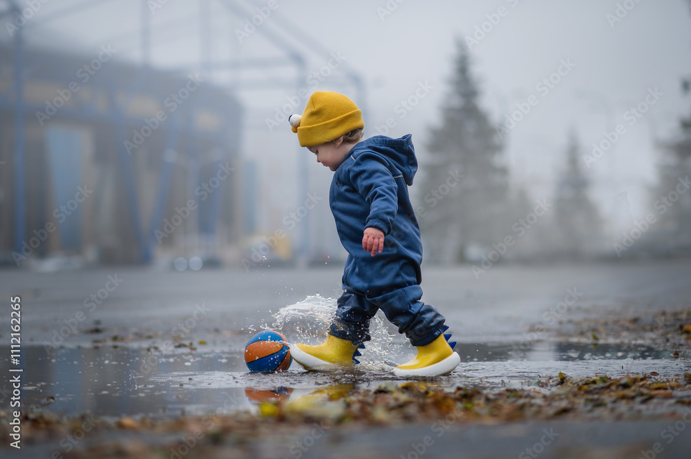 Happy toddler walks through the puddles in blue jumpsuit with splashes ...