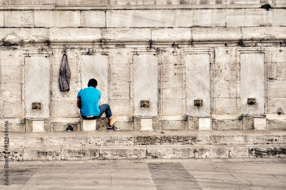 Man in a blue shirt seated near a traditional ablution fountain with ...