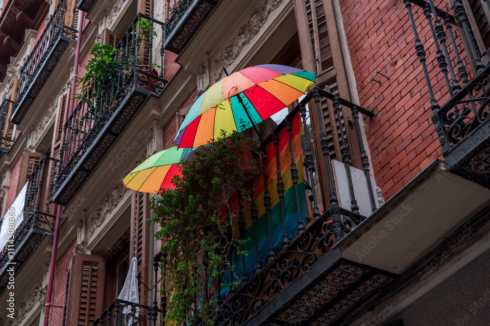 A colorful umbrella is hanging from a balcony. The umbrella is rainbow ...
