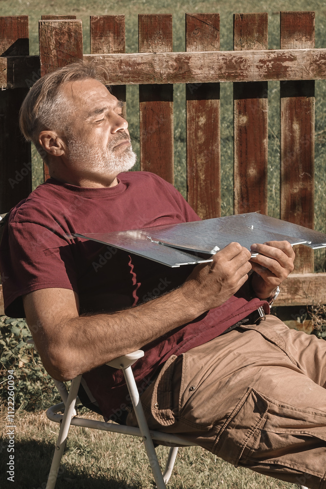 funny scene man sunbathing in the garden with a reflector to attract ...