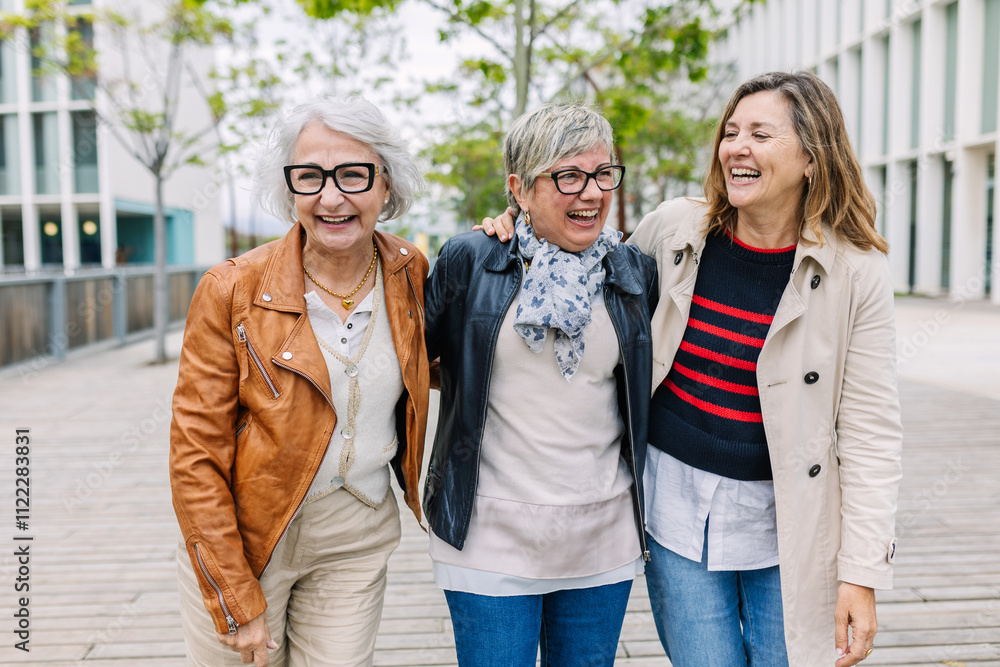 Three mature retired women laughing while walking together outside ...