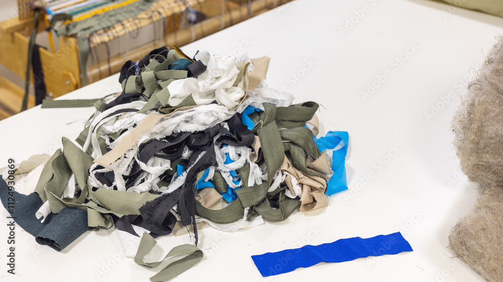 Close-up of textile scraps in focus, with a weaving loom blurred in the ...