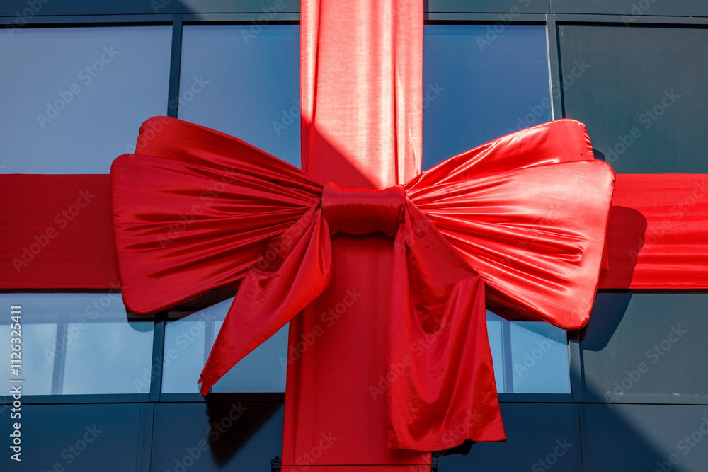 Large red ribbon, tied in a bow, drapes across a modern building's ...