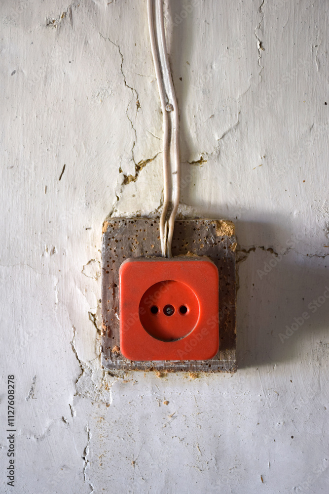An antique electrical socket on a rotten wall with peeling paint ...