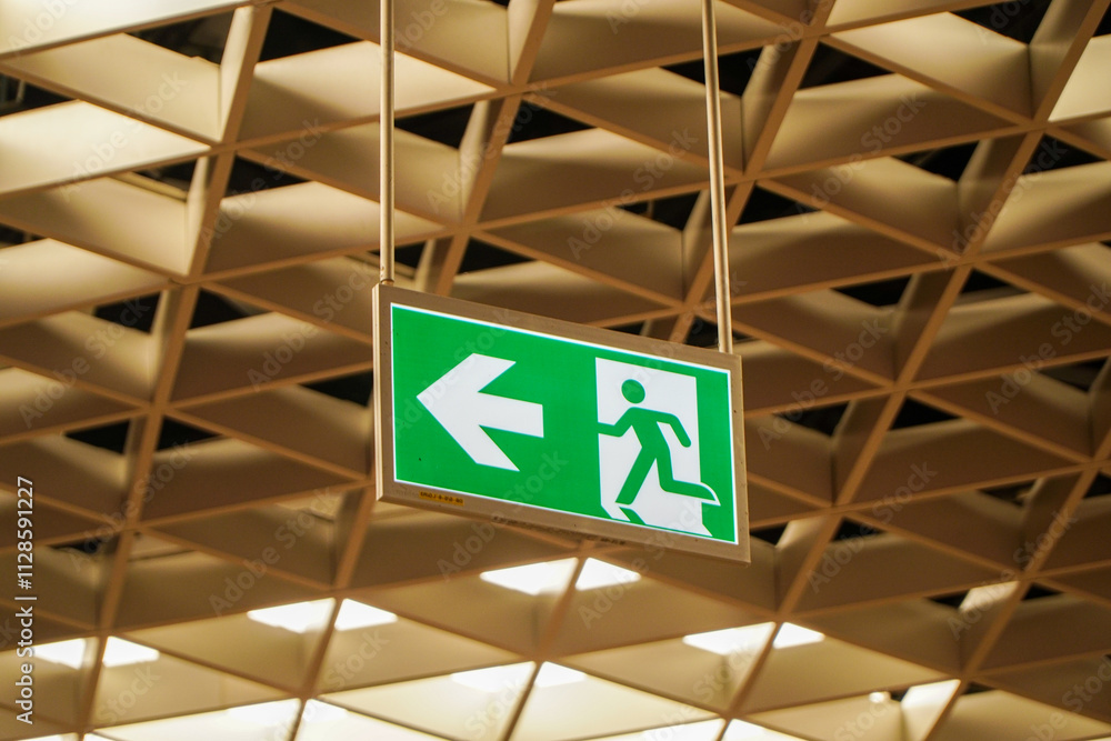 A green emergency exit sign hangs from the ceiling of a building. The ...