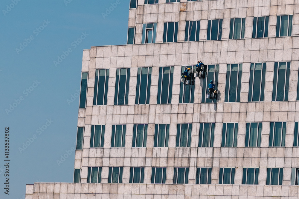 Window washers diligently cleaning a skyscraper facade under a bright ...