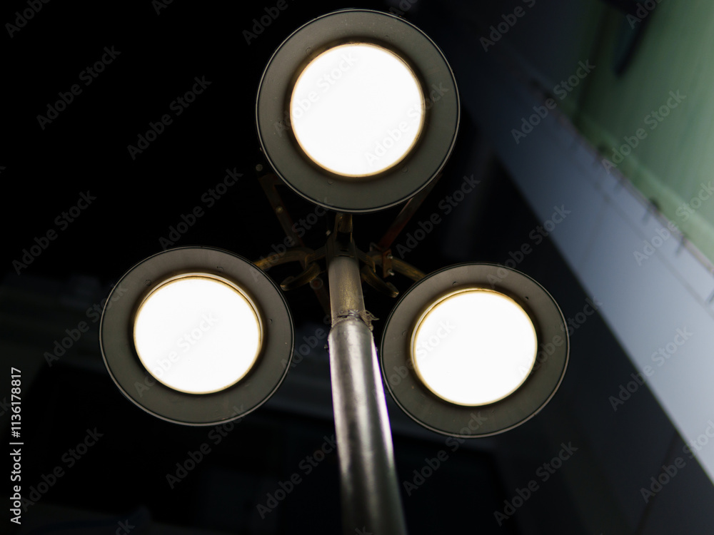 Three bright circular street lights shine down from a metal pole ...
