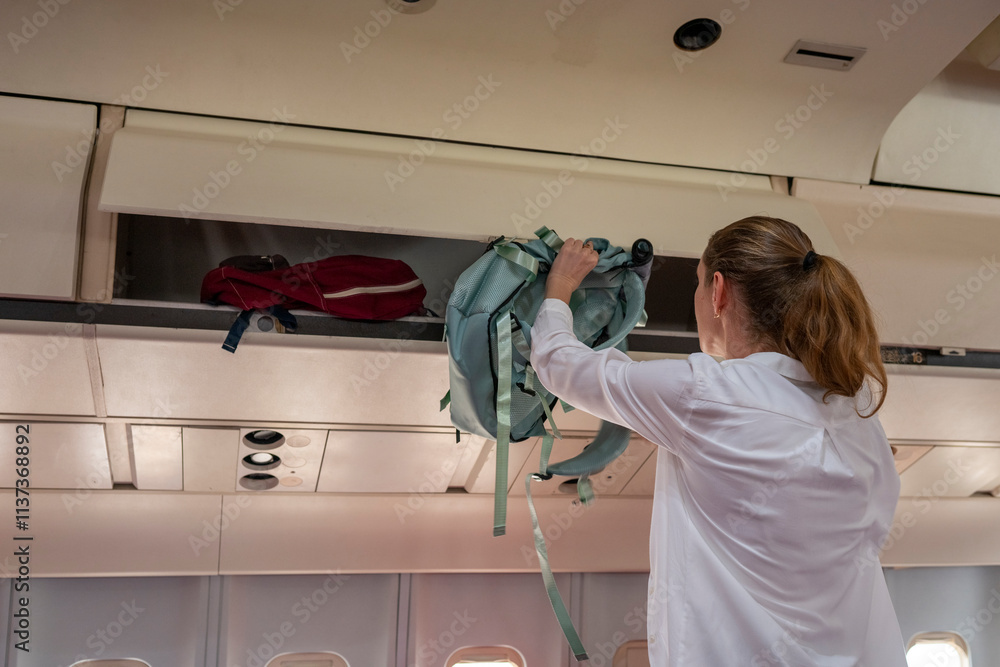 Tourist airplane placing backpack into an airplane's overhead ...