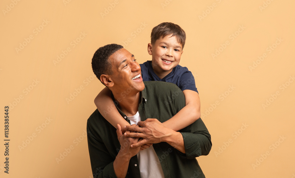 A father playfully embraces his son from behind, both sharing bright ...