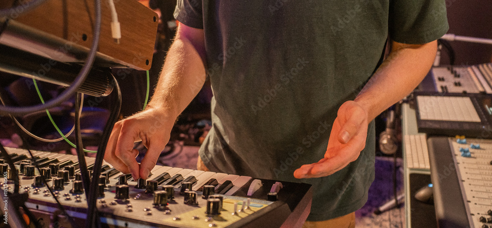 music producer adjusting knobs on a synthesizer in a recording studio ...