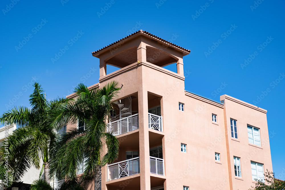 Apartment building with open balconies and palm tree. Low angle view of ...