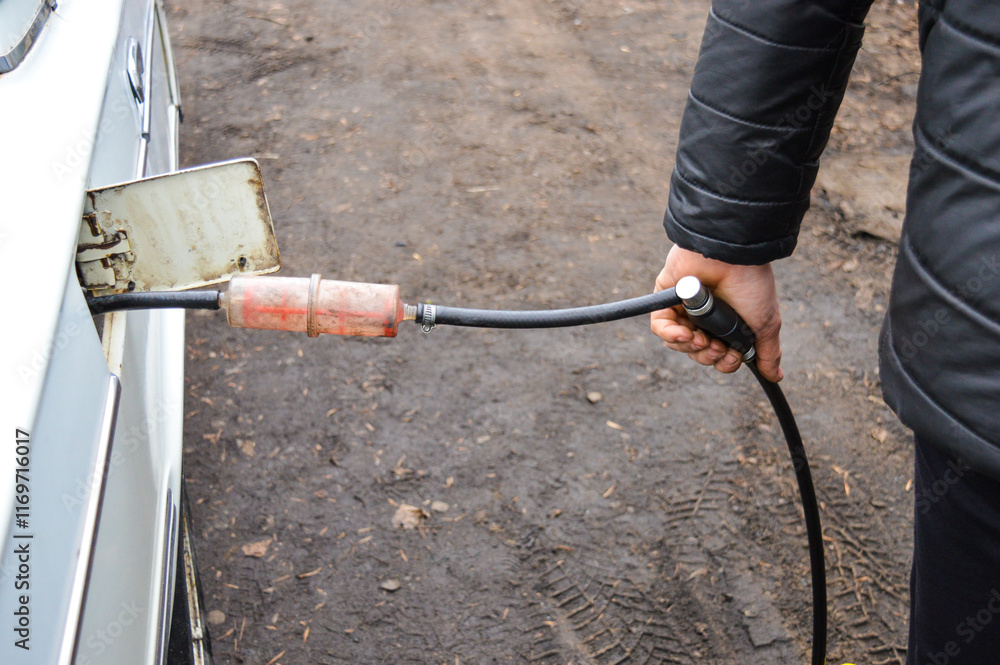 siphoning fuel from an old white car into a transparent plastic bottle ...