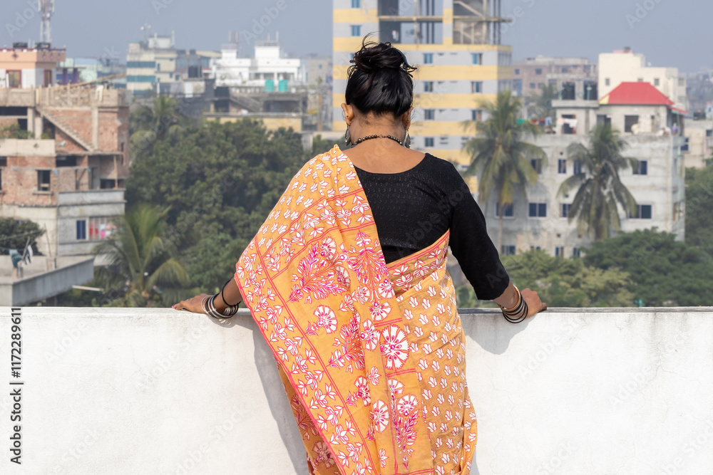 A Bengali woman draped in a floral printed cotton saree, stands alone ...