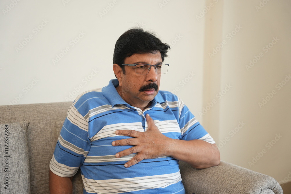 mature indian man having chest pain while sitting on sofa at home ...