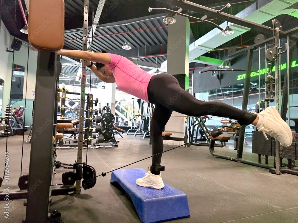 Rear view of 40 year old asian woman doing exercises for glutes, cable ...