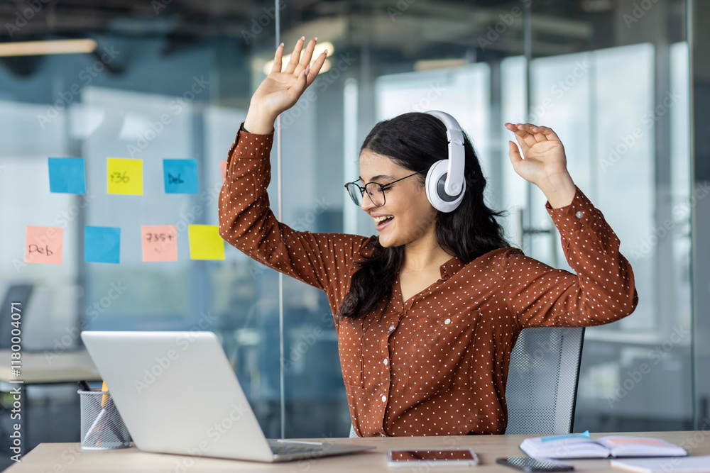 Joyful woman listening to music at workplace in office interior ...