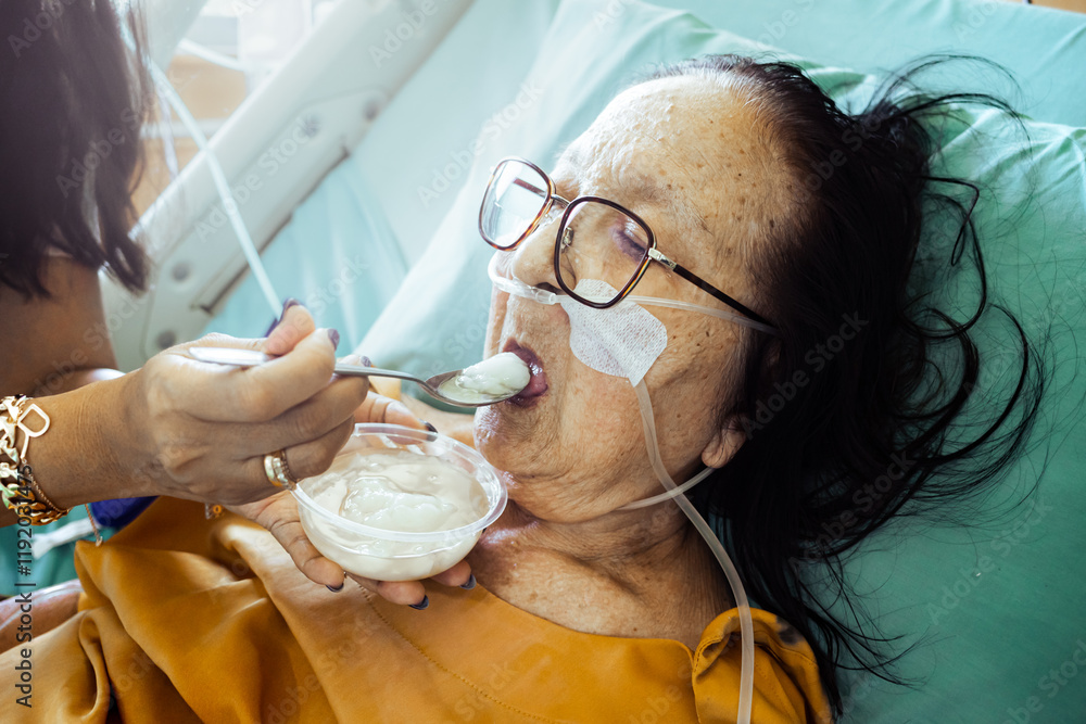 Sick Southeast Asian elderly female patient in hospital bed being feed ...
