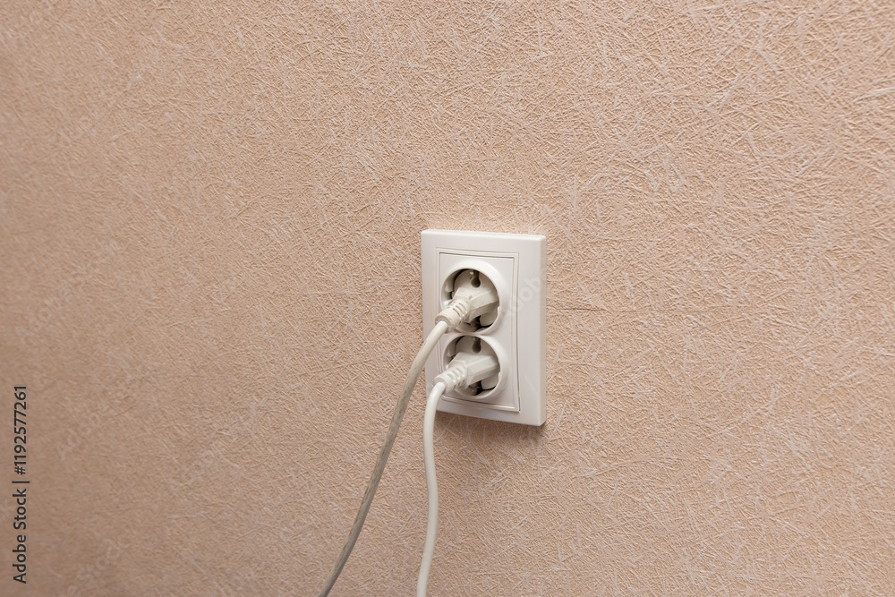 Double electrical outlet with two plugs inserted into a beige textured ...