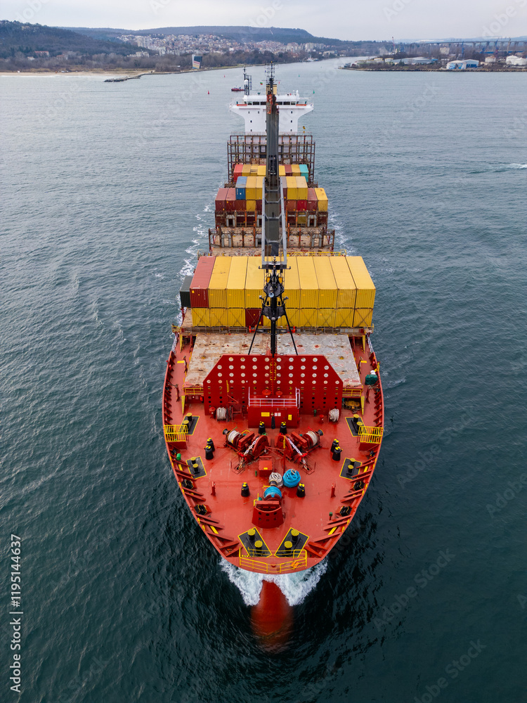 Front aerial view of a red container ship sailing through calm waters ...