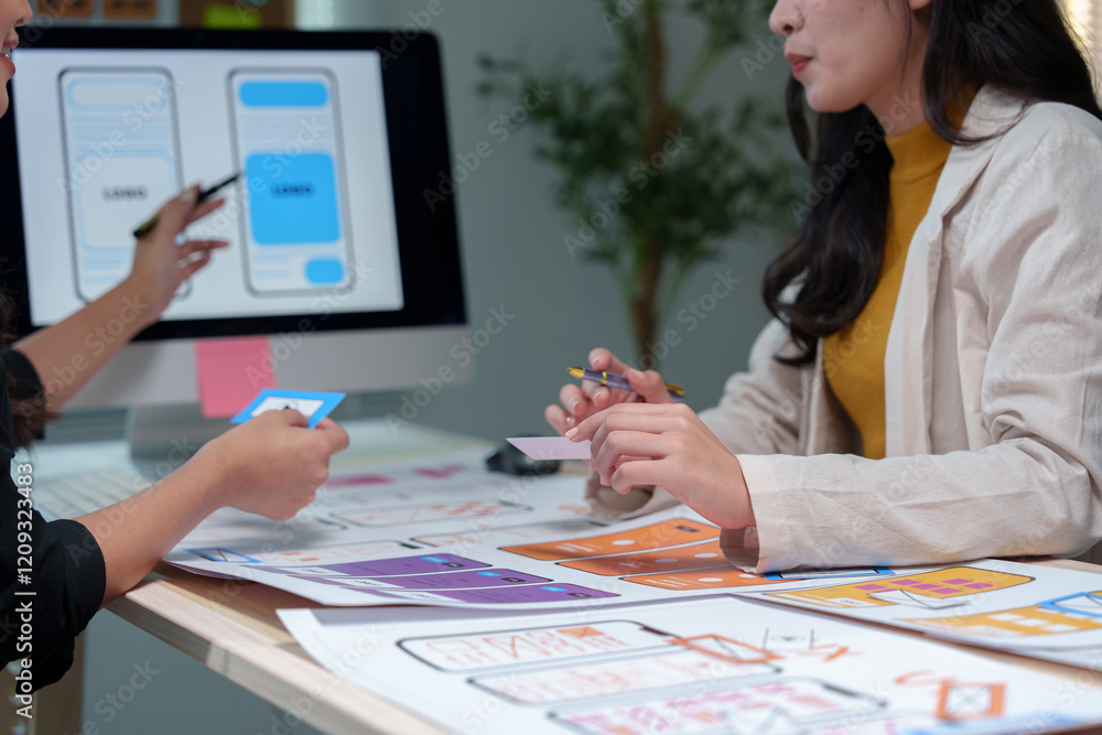 Two Asian Female Web Designers Collaborating On Mobile App Interface Wireframe Design At A Desk
