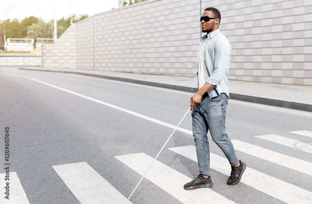 Young black visually impaired man wearing dark glasses, walking across ...