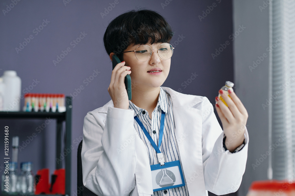 Asian female healthcare professional examining small vial while talking ...