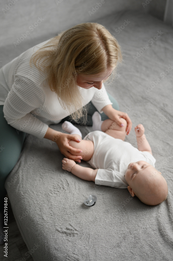 Woman does gymnastics to newborn baby lying on back on bed, spreading ...