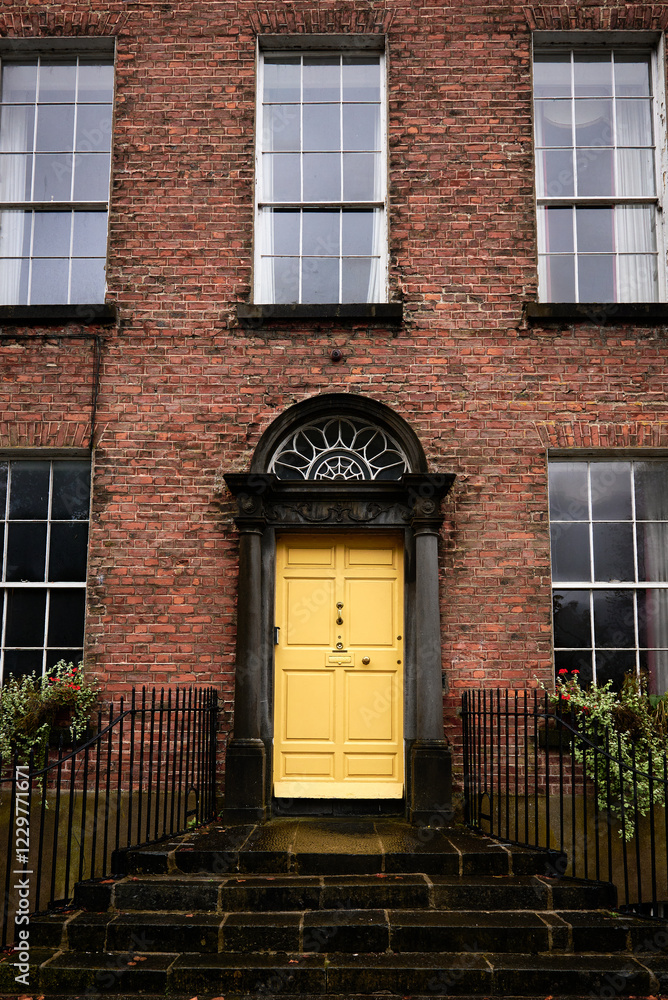 A vibrant yellow door set in a historic Georgian-style brick building ...