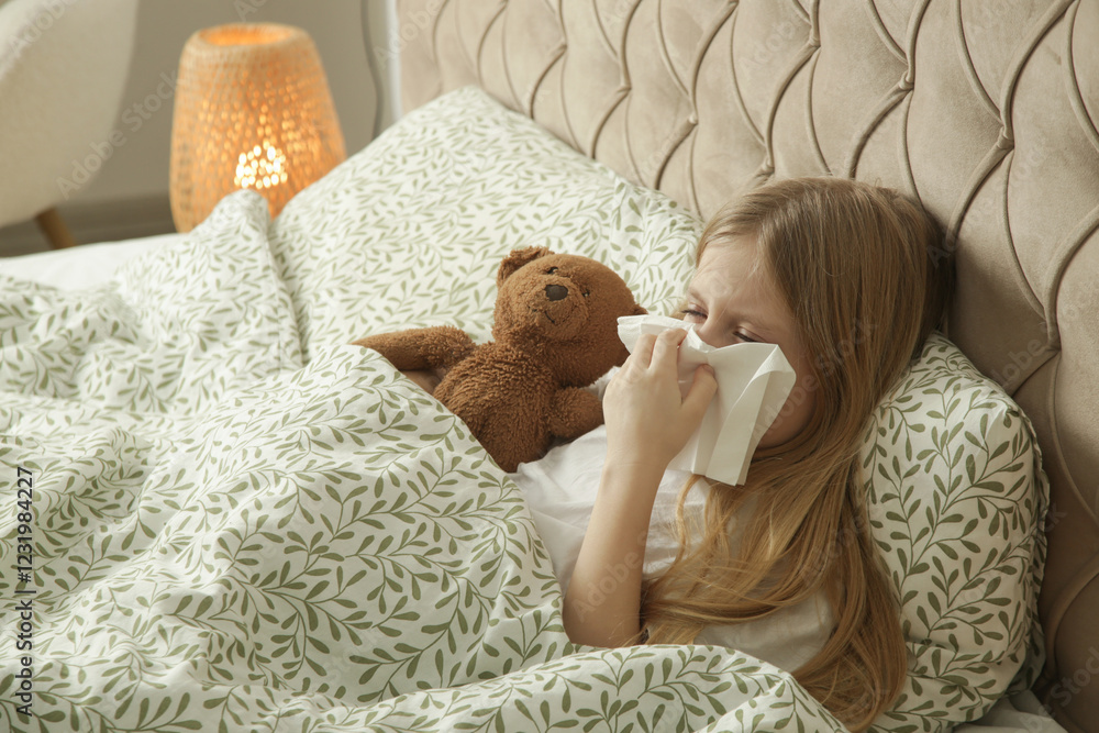 Little 7 year old girl with influenza is sitting in bed and blowing her ...