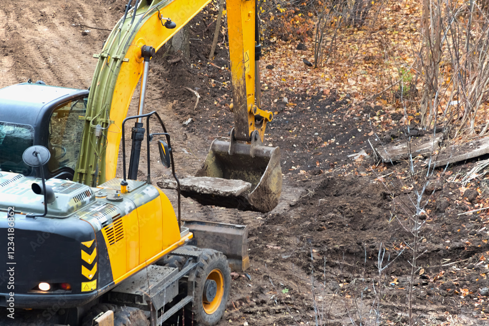 The bucket of a backhoe excavator is lifting a concrete slab on a ...