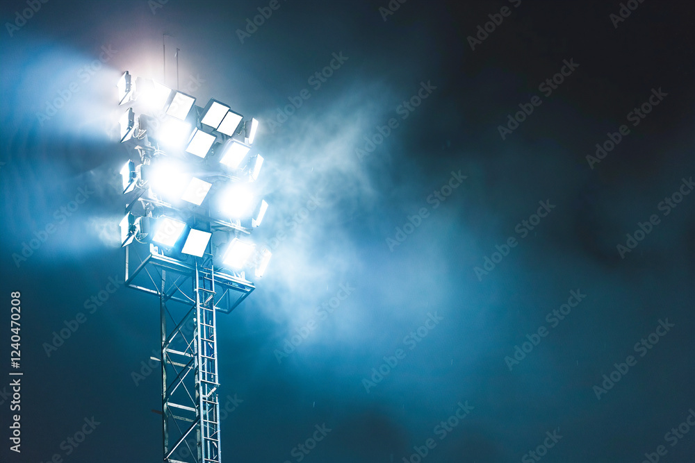 Intense stadium floodlights break through the dense fog, creating a ...