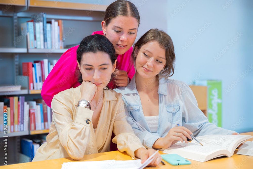 Three young women collaborating at a library table, studying and ...