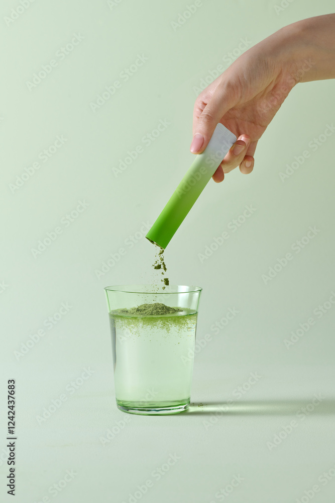 Hand Adding Green Powder Mix Into a Glass of Water on Plain Background ...