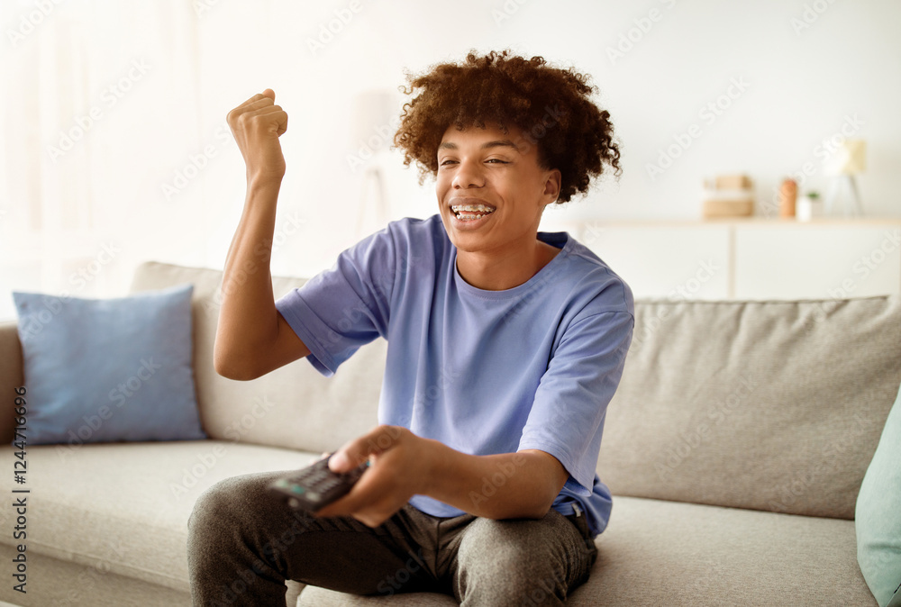 Excited African American teen with remote control enjoying movie ...