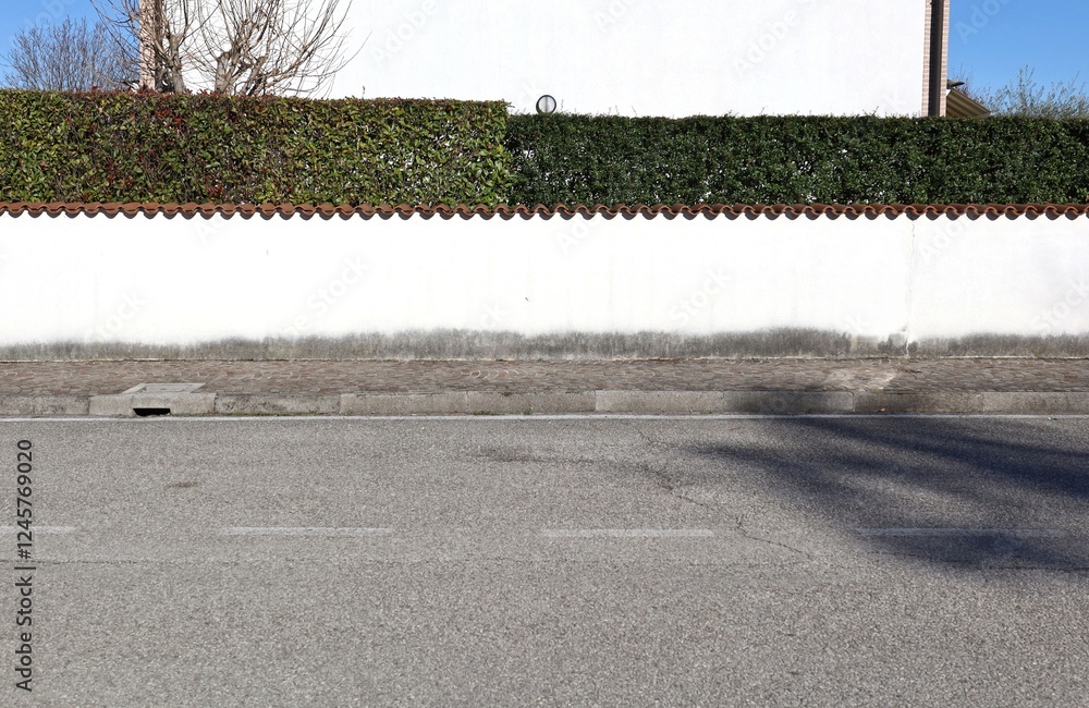 White plaster fence with a row of roof tiles on top. Sidewalk and ...
