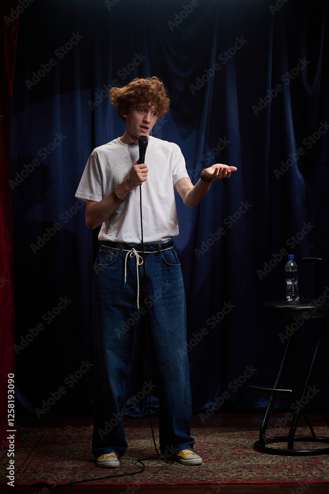 Young comedian delivering a standup performance on stage while holding ...