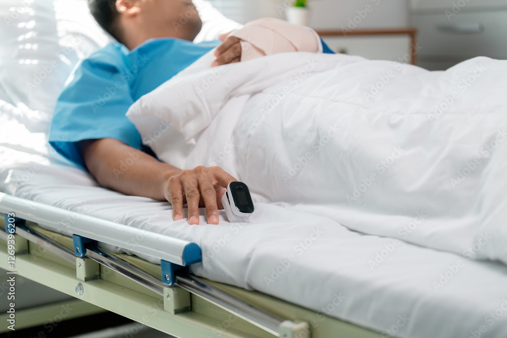Asian patient lying in hospital bed, wearing pulse oximeter ...