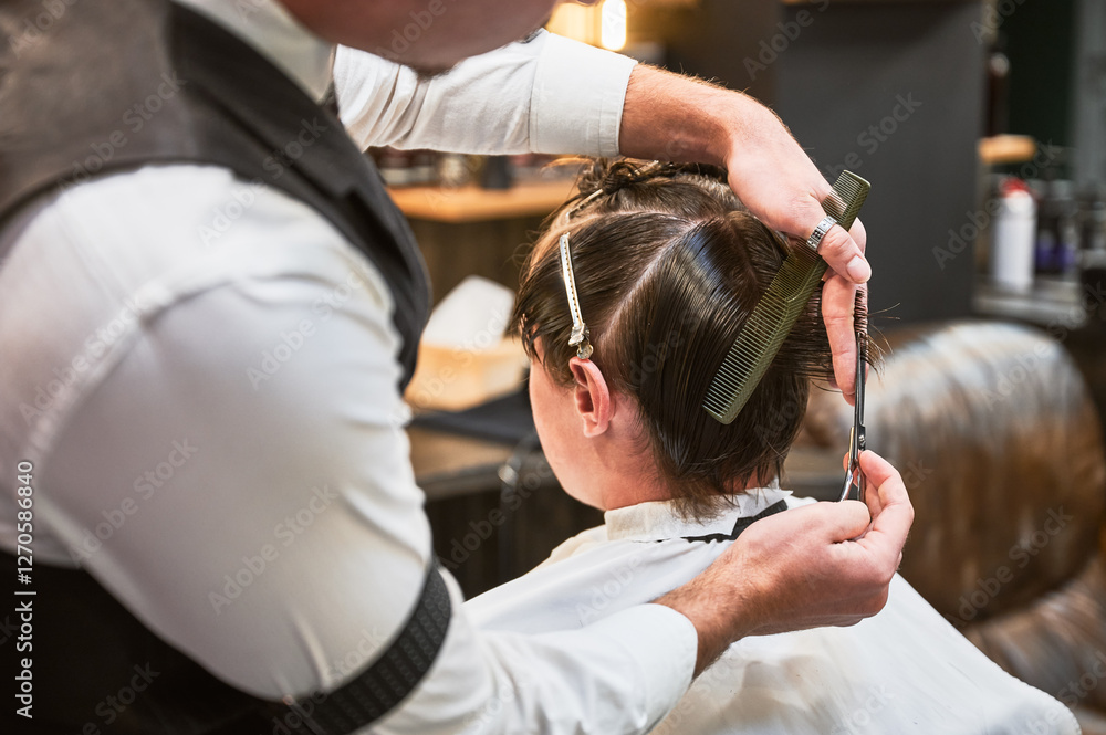 Back view of barber in fancy outfit cutting wet hair. Young client ...