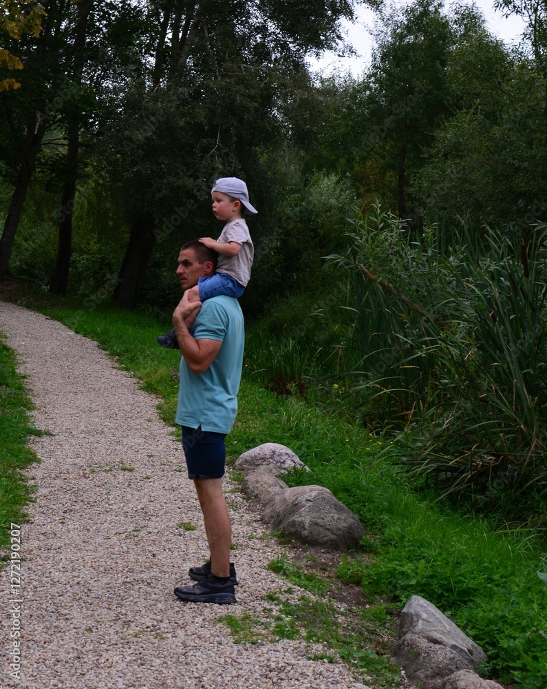 Father carrying his boy on neck outside in summer. Son sits on his dads ...