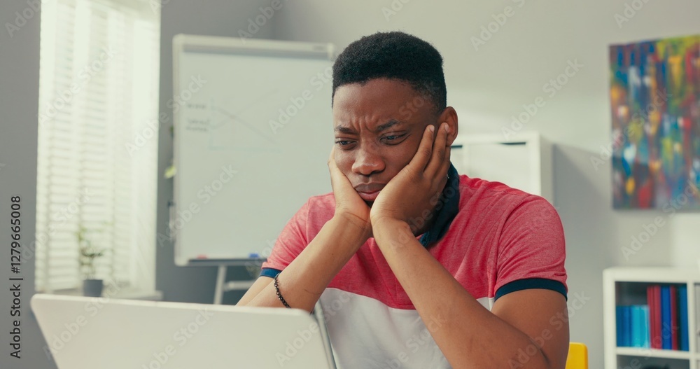 Young dark-skinned boy sits slumped in front of computer, props hands ...