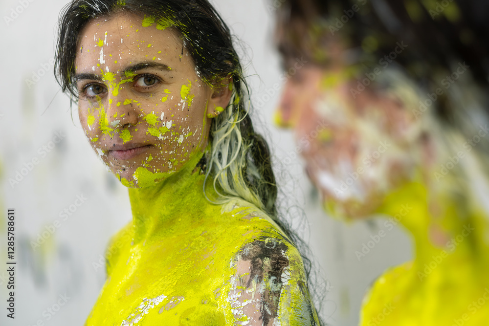 Woman covered in vibrant yellow and black paint gazes confidently into ...