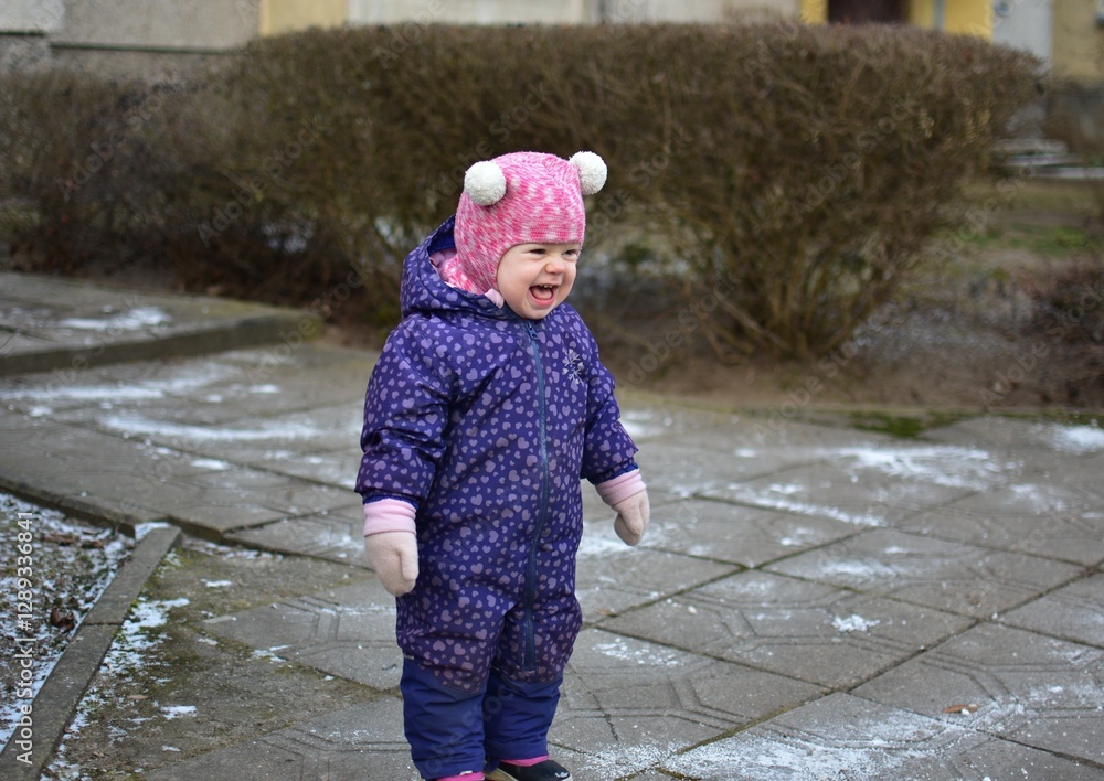 Baby girl standing next to entrance to the apartment house with winter ...