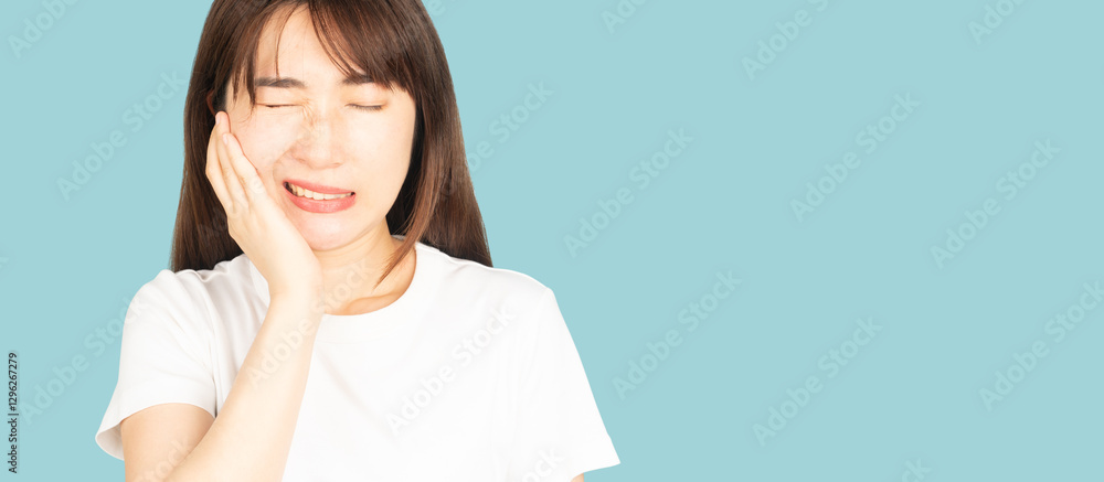 Asian woman suffering from toothache or jaw pain over blue background ...