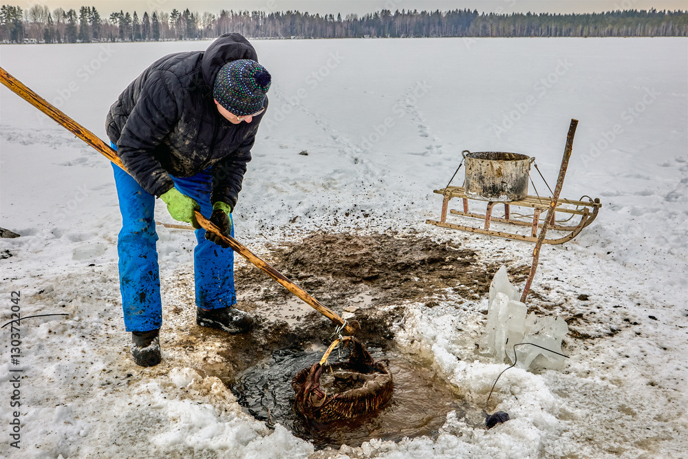 Farmer extracting sapropel from a freshwater lake through an ice hole ...