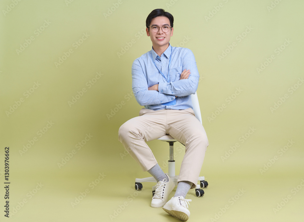 Young man seated on a chair with a relaxed pose against a light green ...