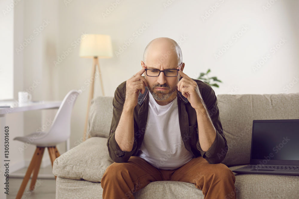 Serious confused puzzled man sitting on sofa with laptop computer at ...