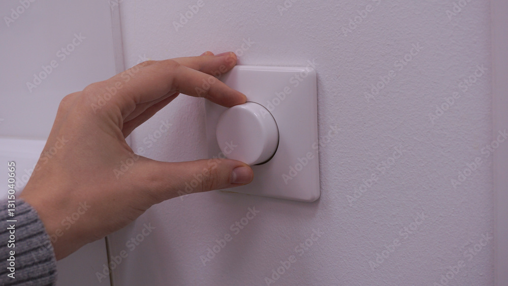 Hand adjusting brightness or turning down electrical light dimmer ...