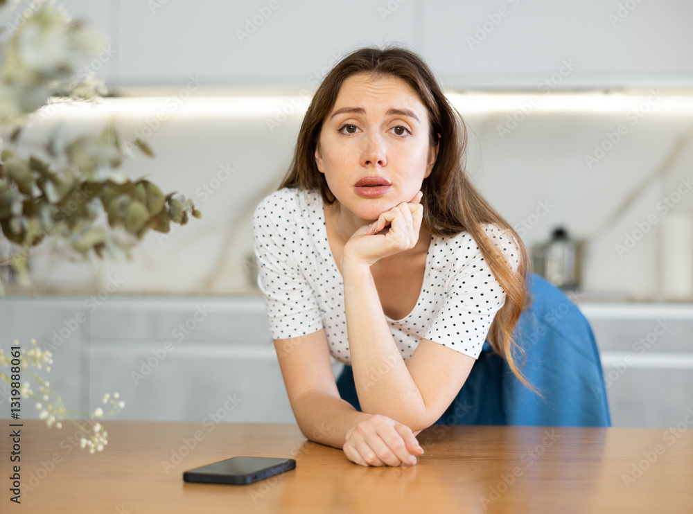 Bored middle-aged woman bending over table looking thoughtfully at her ...